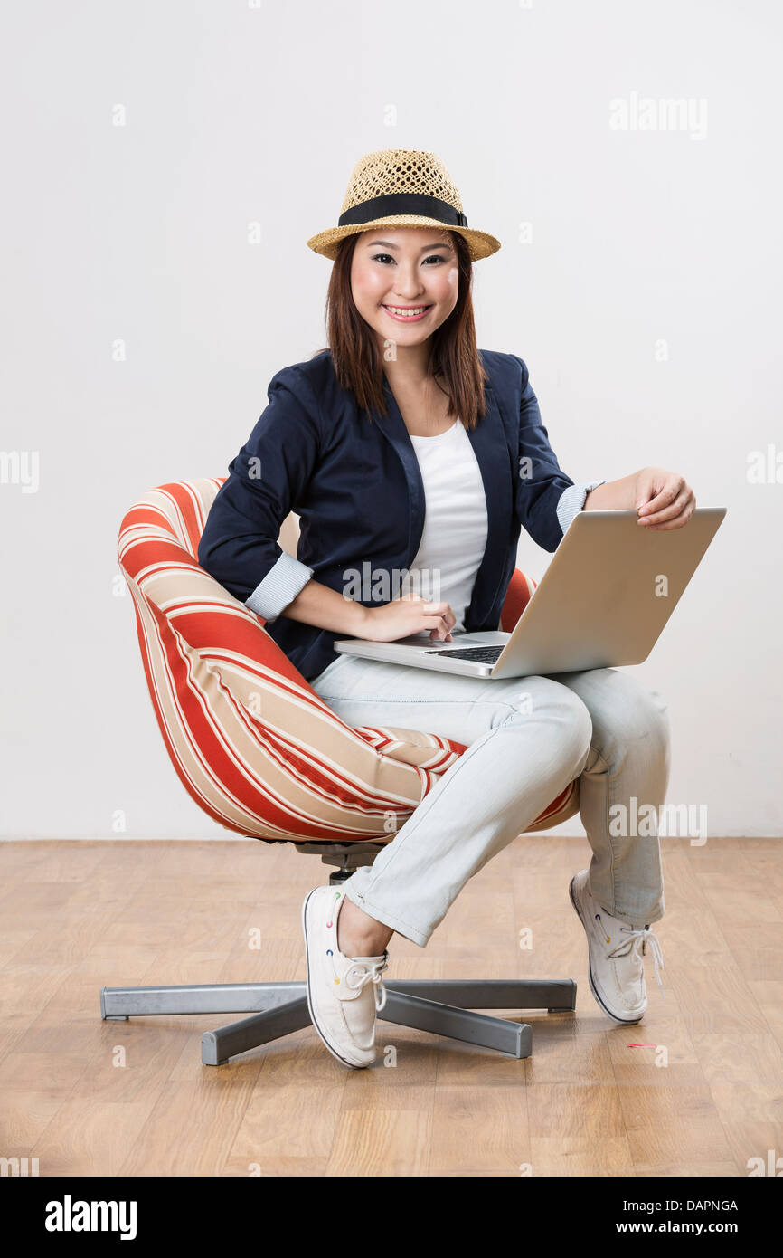 Portrait of a happy Chinese woman sitting on a chair using Digital ...