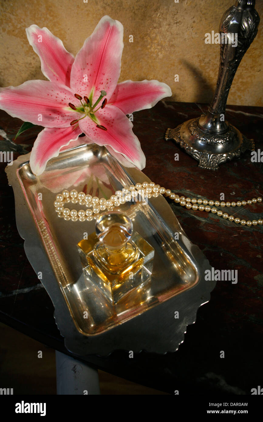 feminine still life with perfume bottle, pearls and flower on silver ...