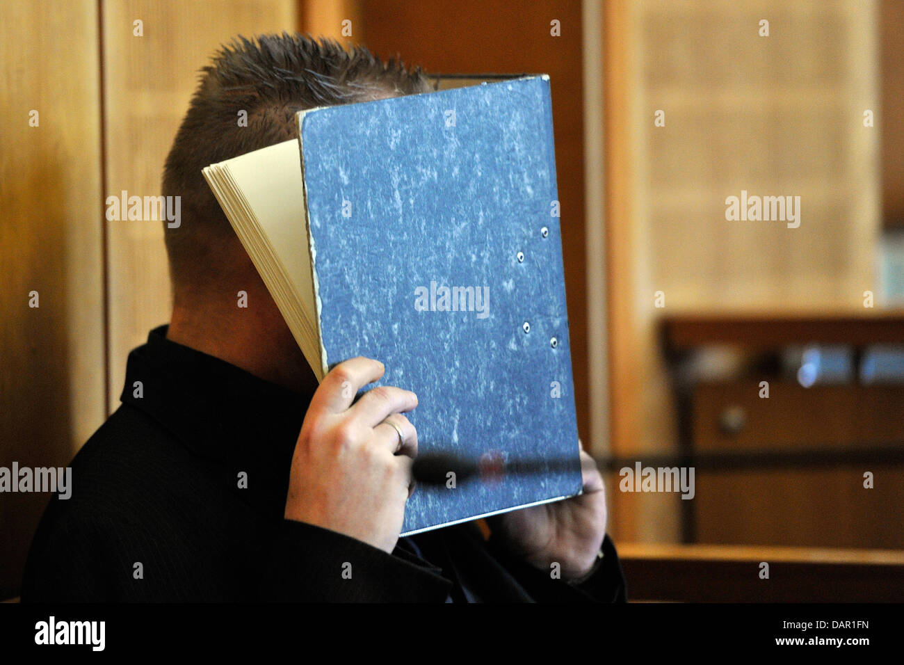 The accused Olaf H. hides his face behind a file in the court room of ...