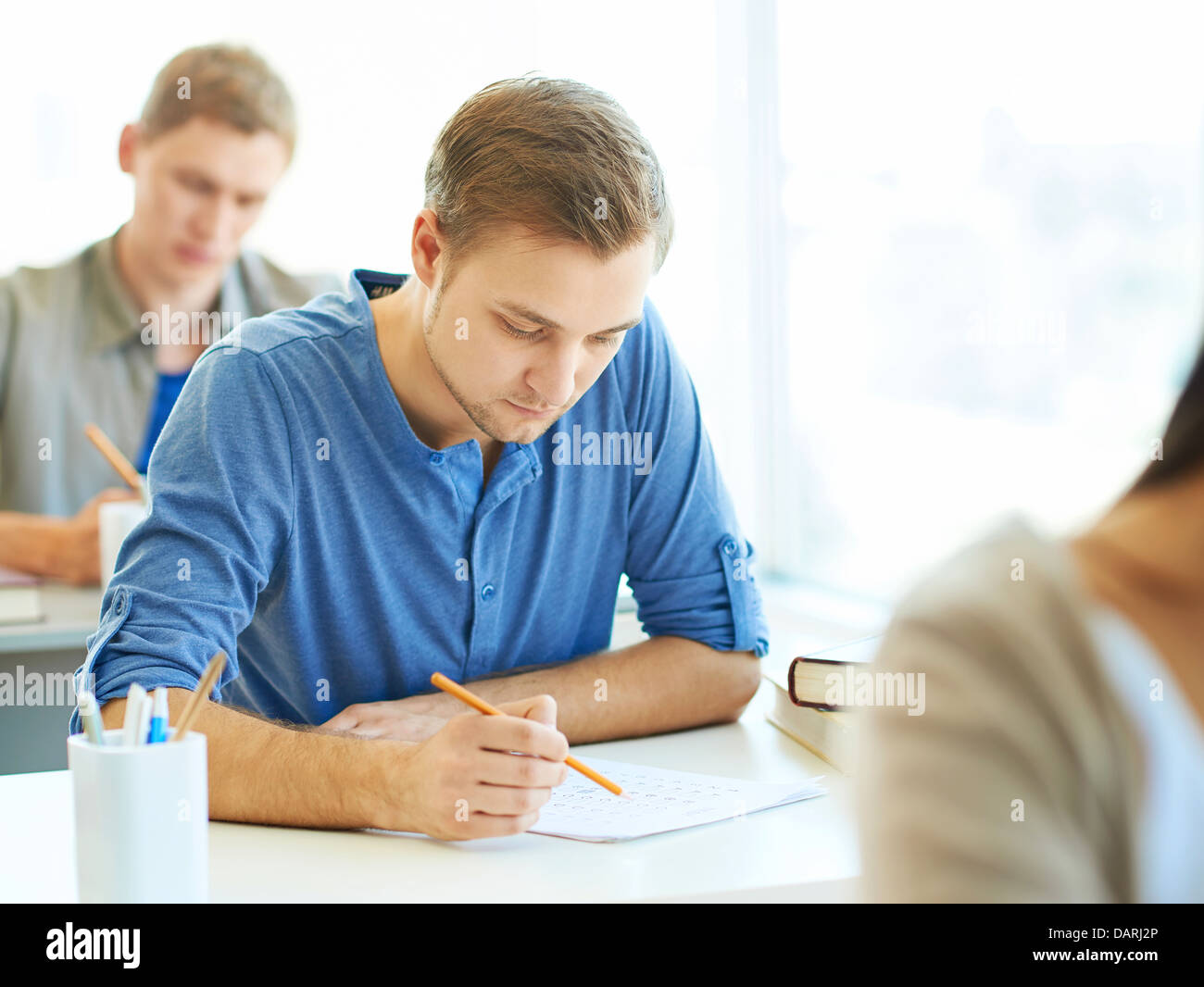 Portrait of handsome student carrying out test at lesson with groupmate ...