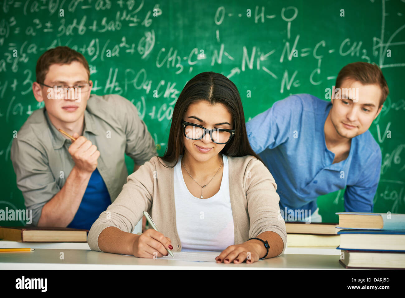Portrait of smart student carrying out test with two guys behind ...