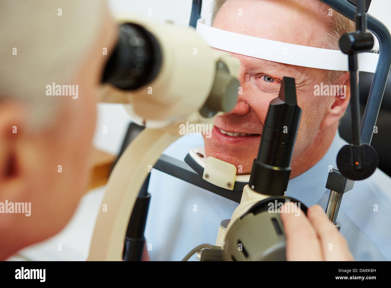 Senior man at optician looking in slit lamp to get his cornea examined ...