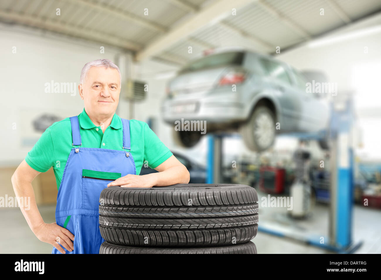 Auto mechanic posing on tires in front of car during automobile ...