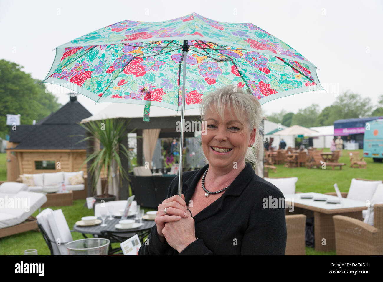 A stallholder on a garden furniture stand under an umbrella in the rain ...