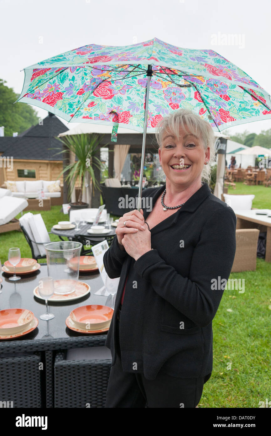 A stallholder on a garden furniture stand under an umbrella in the rain ...
