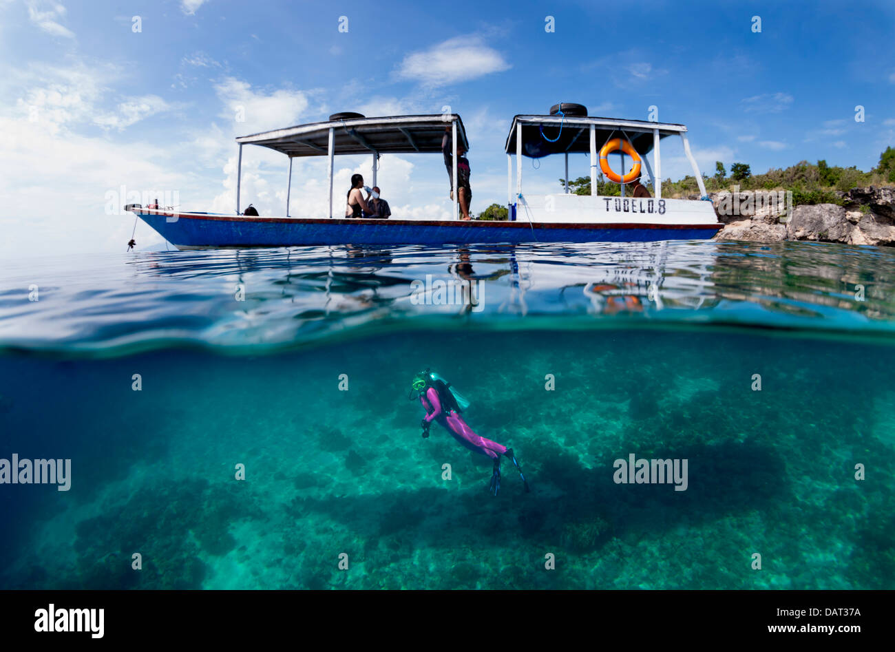Split level view of blonde female diver exploring reef below dive boat ...