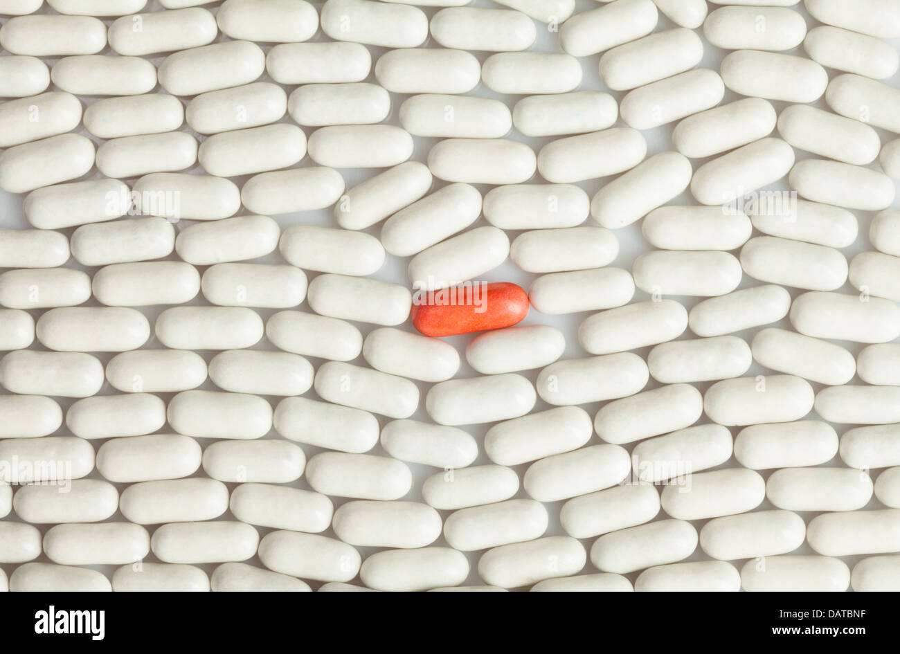 Many same white pills in a row pattern with one red drug laying between ...