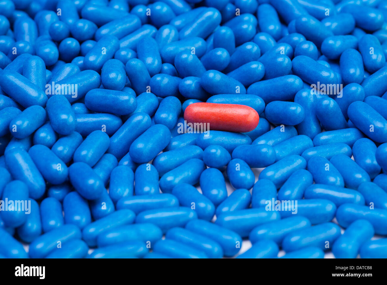 Red drug pill laying on big pile of blue tablets Stock Photo - Alamy