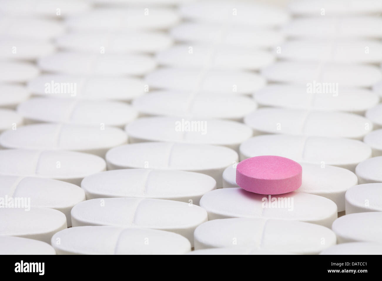One pink red tablet laying on many big white drugs laying in a row ...