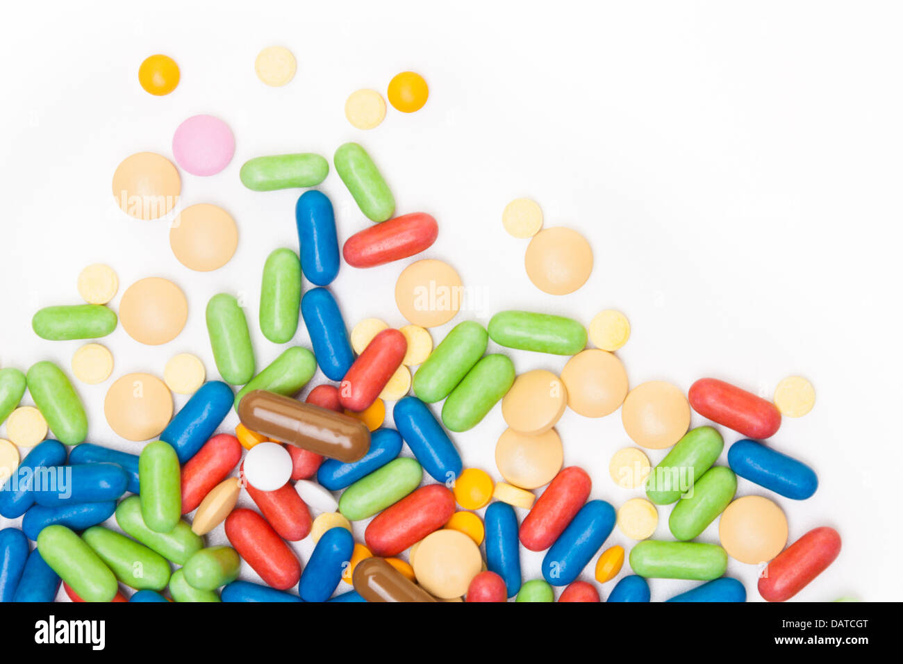 Pile of pills and tablets of different color laying on white table ...