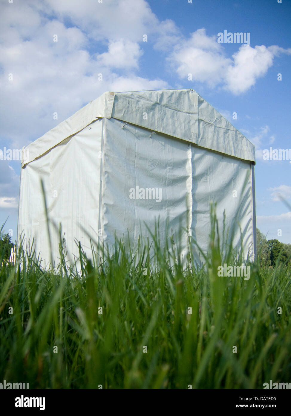 Plain white tent in grassy field. Faint type marks leading up to tend ...