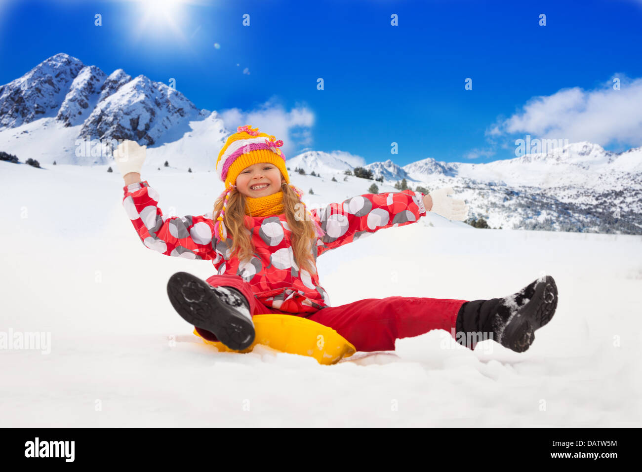 Happy, smiling girl sitting on sled with her hands lifted, with ...
