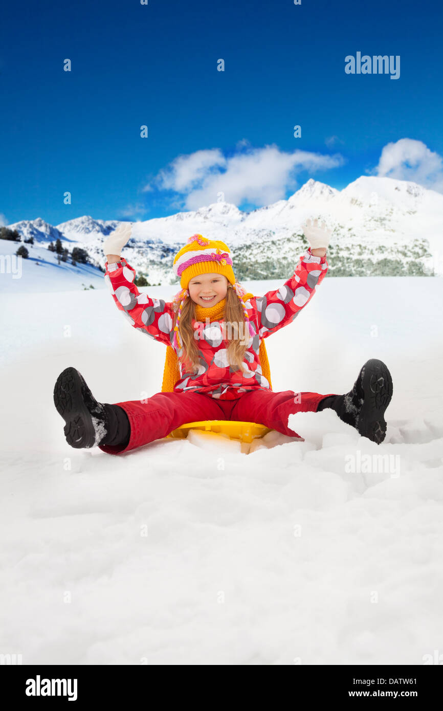 Smiling, smiling girl sitting on sled with her hands lifted, in the ...