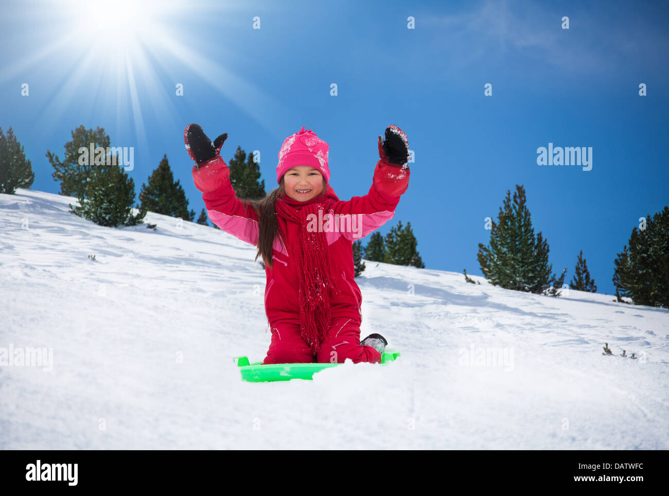 Happy, smiling girl sitting on sled with her hands lifted, on slide in ...