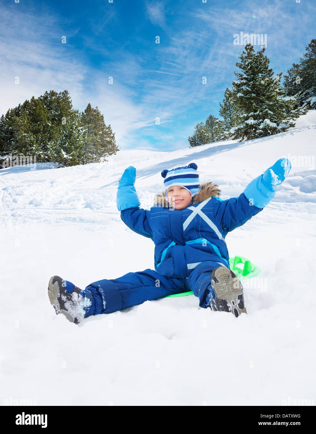Happy, smiling boy sitting on sled with her hands lifted, on slide in ...