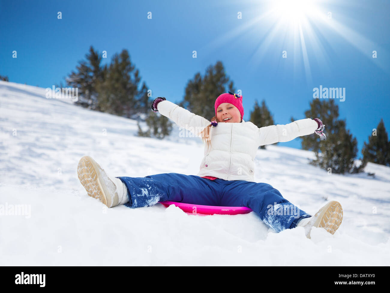 Happy girl sitting on sled with her hands lifted, wearing ski mask, in ...