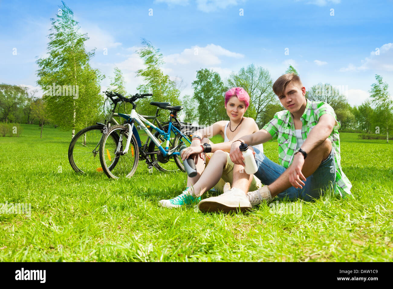 Beautiful young couple sitting on the grass with bikes Stock Photo - Alamy