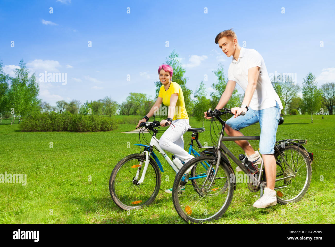 Two young people, man and woman riding a bike in the park Stock Photo ...