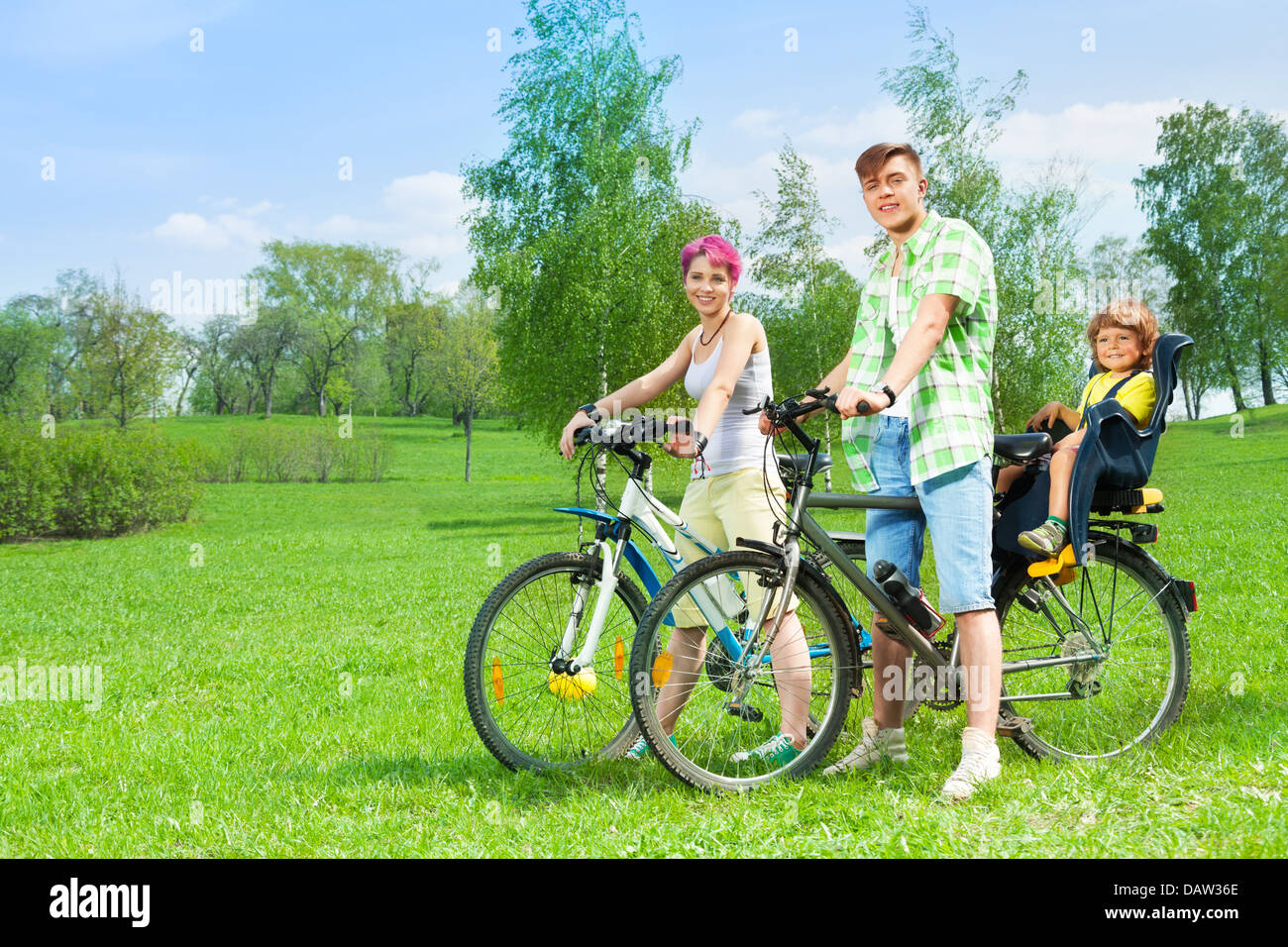 Young family man and woman on the bikes with kid in child seat riding ...