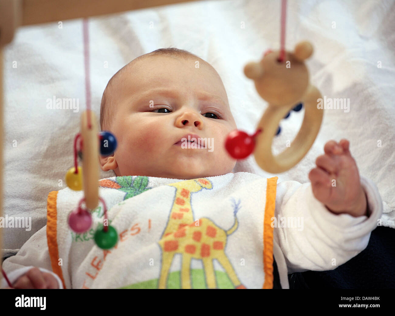 A almost three-year old baby lies in its bed while catching dangling ...