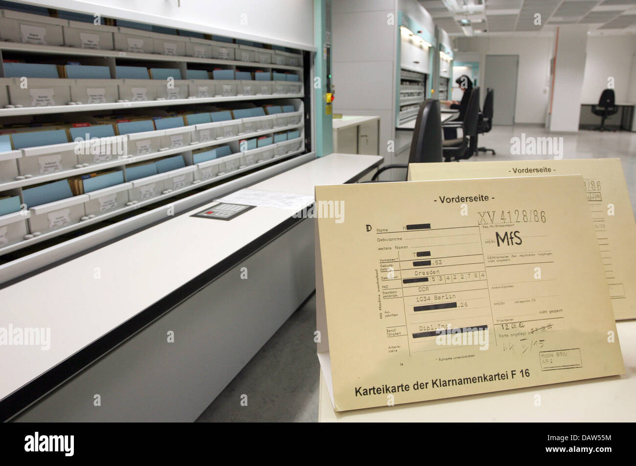 An oversized file card is shown in front of shelves with file cards of ...