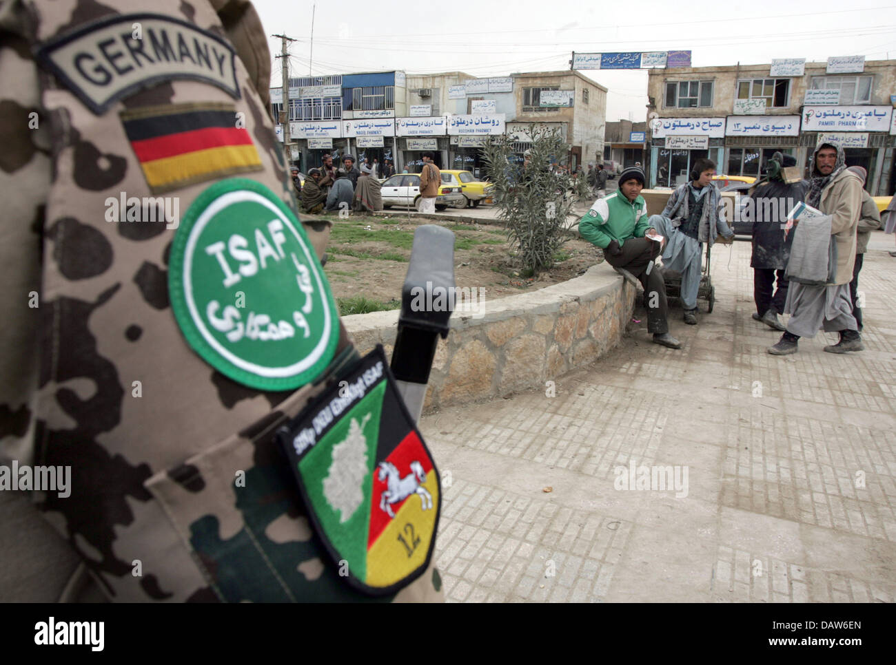 Afghan men in traditional clothes look at a German ISAF soldier in ...