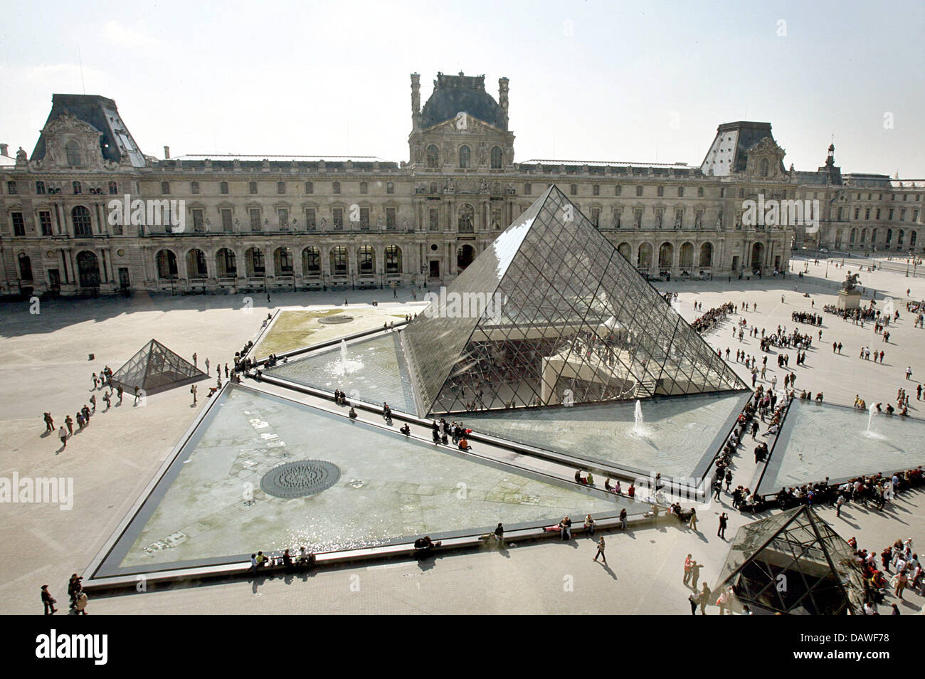 Visitors walk across the courtyard of the Louvre with its glass ...