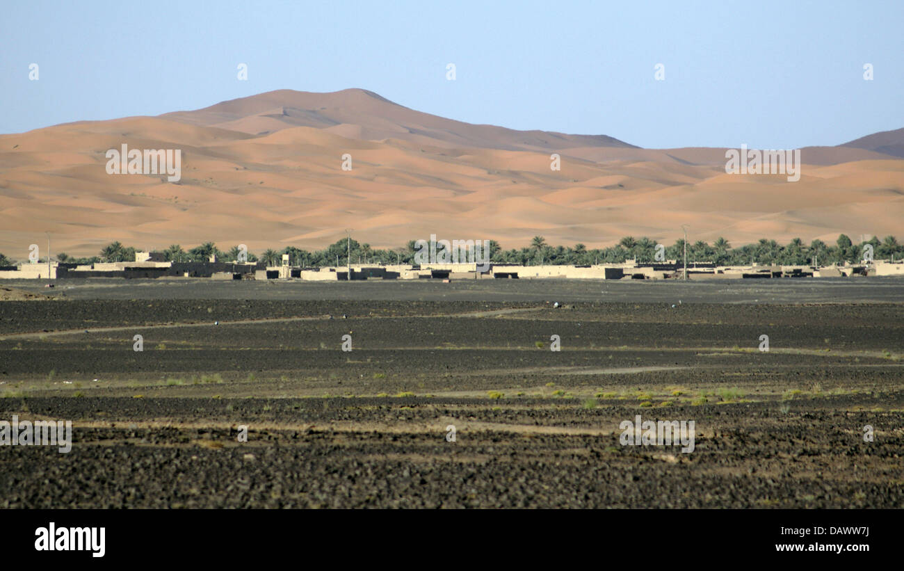 Sand dunes shine brightly behind a plain of dark soil and a clay ...