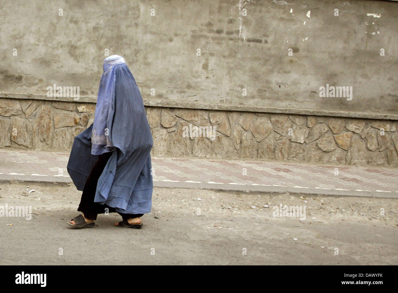 A veiled woman in a blue burqa walks along a street in Kabul ...
