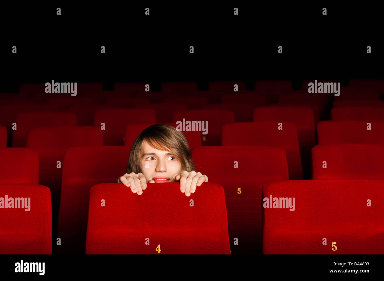 young man in the cinema hiding behind a chair Stock Photo - Alamy