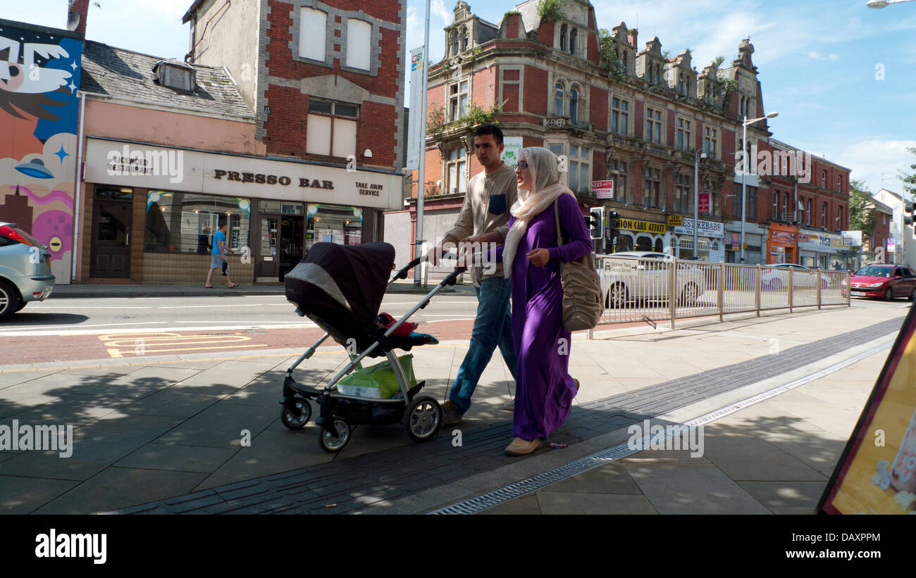 A young Muslim couple walking along street pushing a pram in Swansea ...