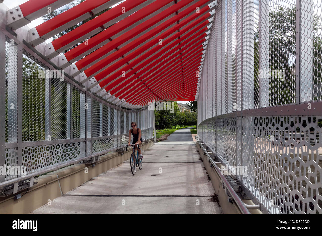 Woman on bicycle crosses orange pedestrian bridge across SW 13th Street ...