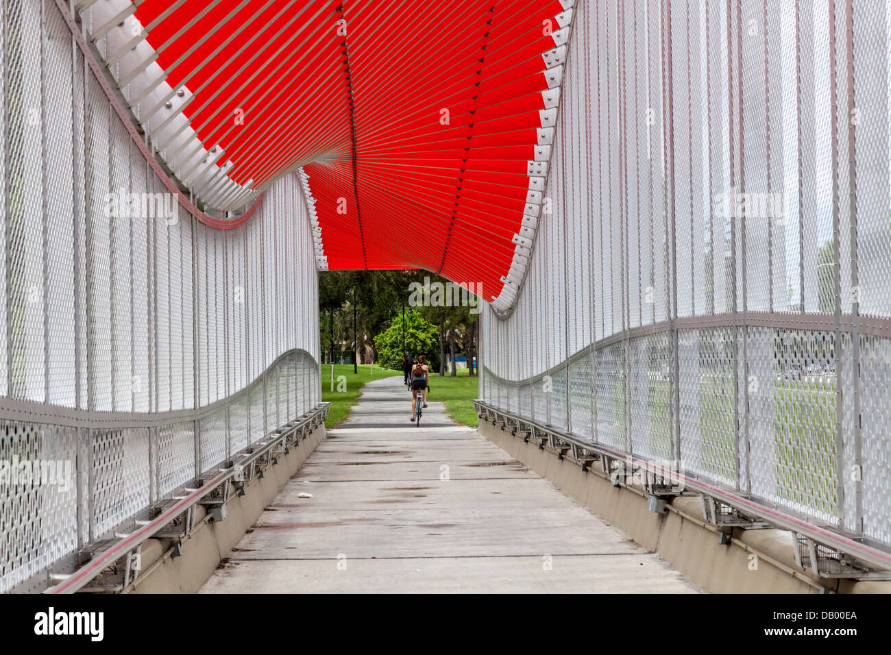 Woman on bicycle crosses orange pedestrian bridge across SW 13th Street ...