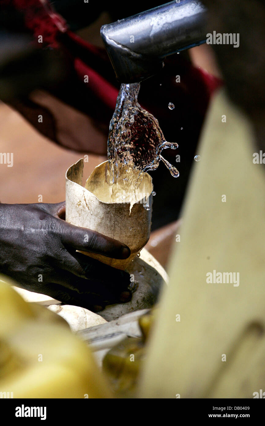 A Refugee uses an old funnel to fill plastic a plastic container with ...
