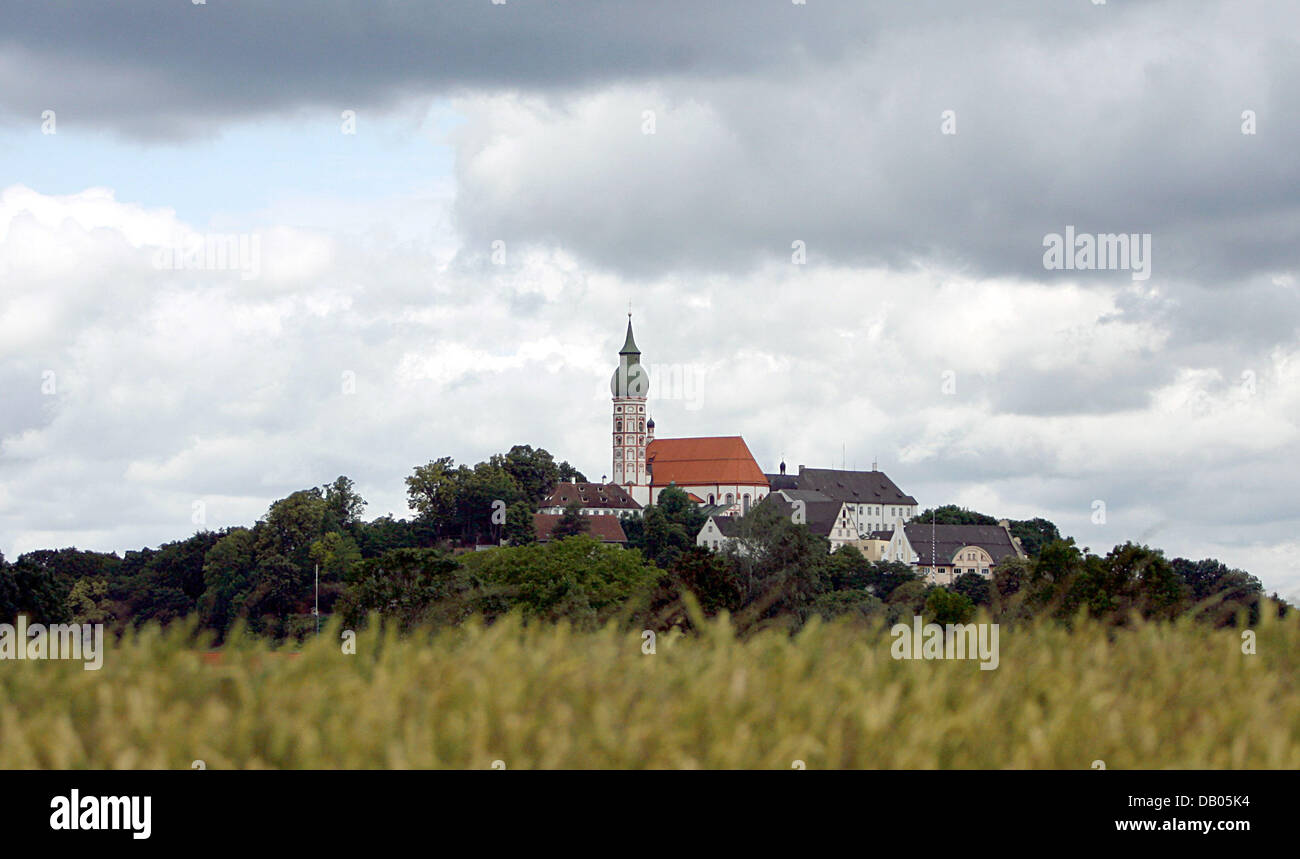 The photo depicts Andechs monastery underneath dark clouds behind corn ...