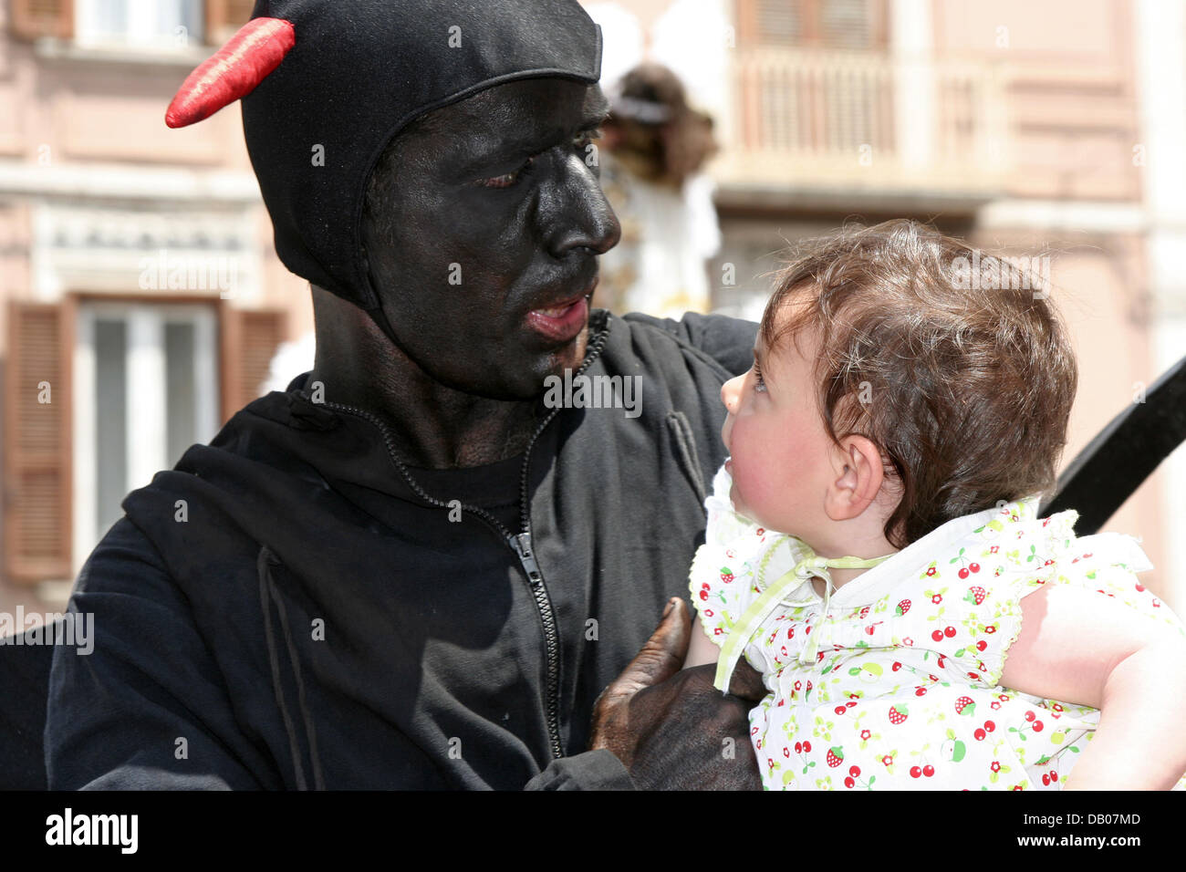 A 'devil' holds a child in his arms during a religious parade in ...