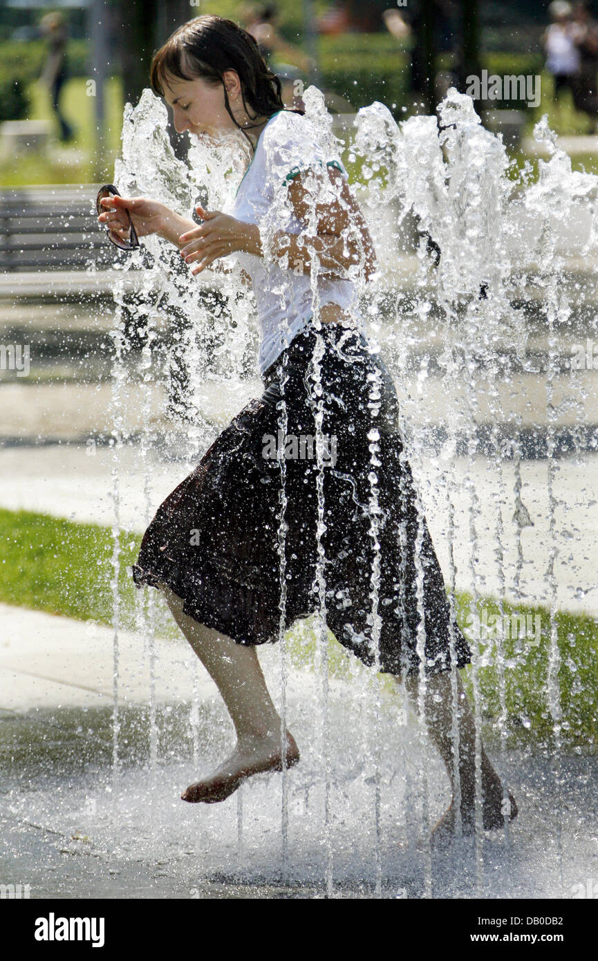 A young woman refreshes herself running through water fountains in ...