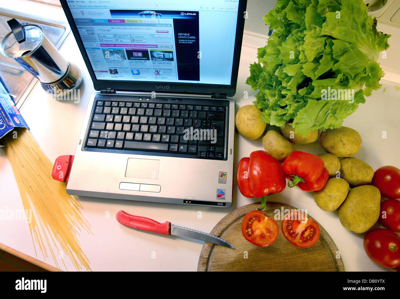 Cooking utensils are placed around a switched on laptop at a kitchen in ...