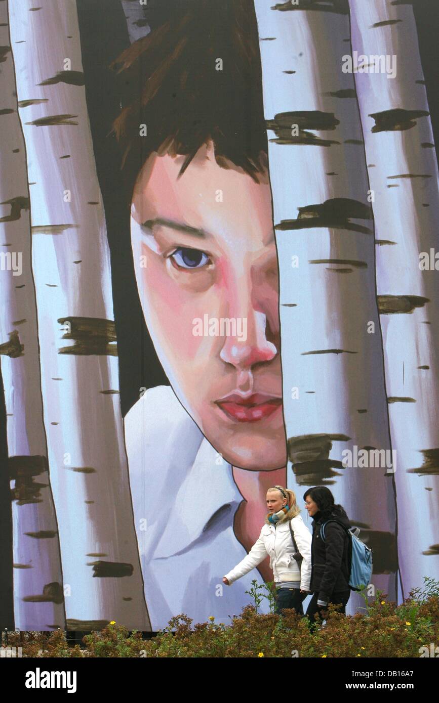 Young women walk past a giant painting by British artist Christopher ...