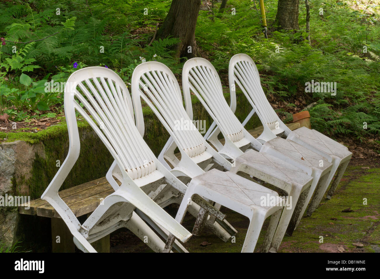 Four white plastic chairs and side tables lean up in a row against a ...