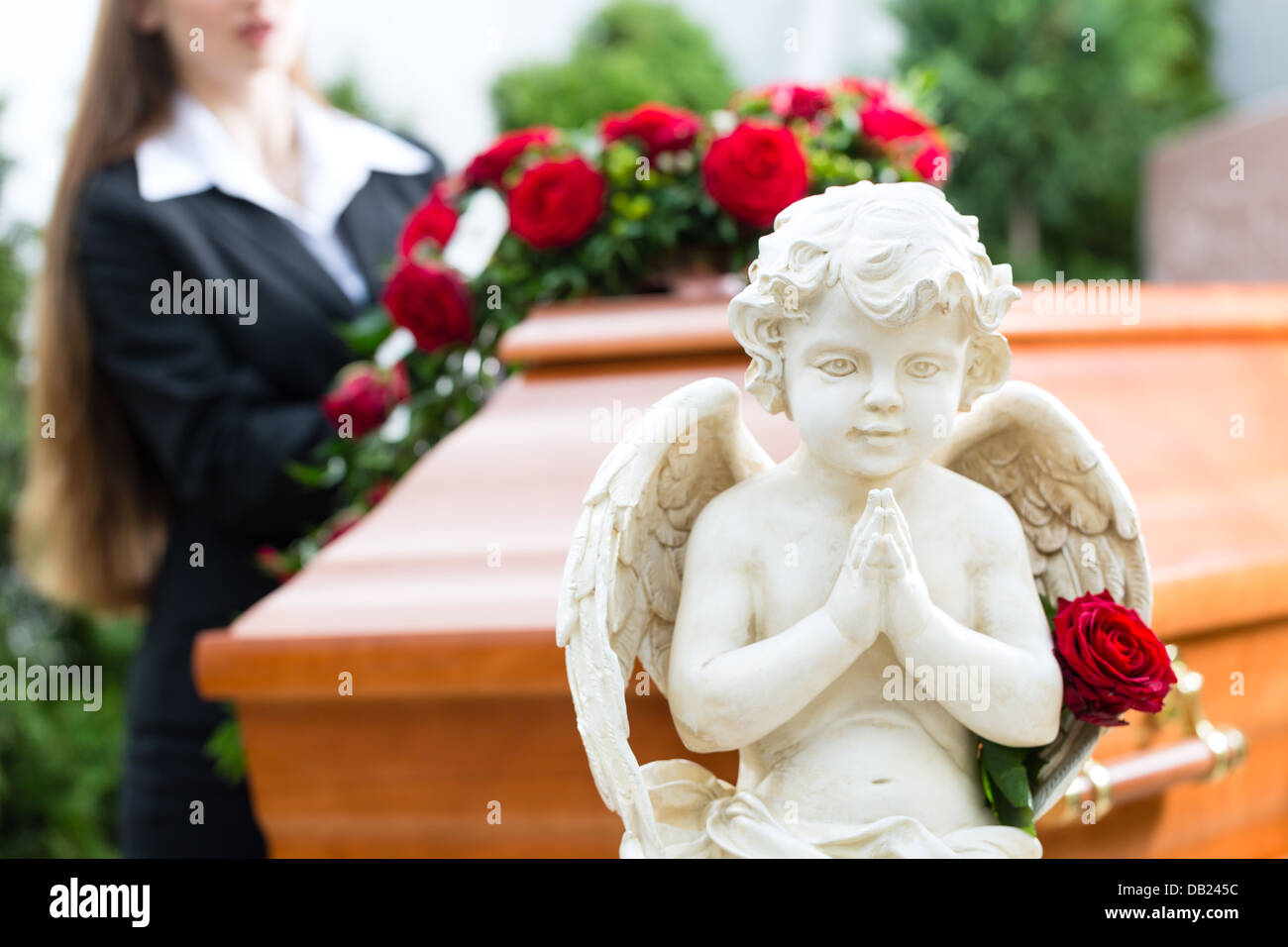 Mourning woman on funeral with red rose standing at casket or coffin ...