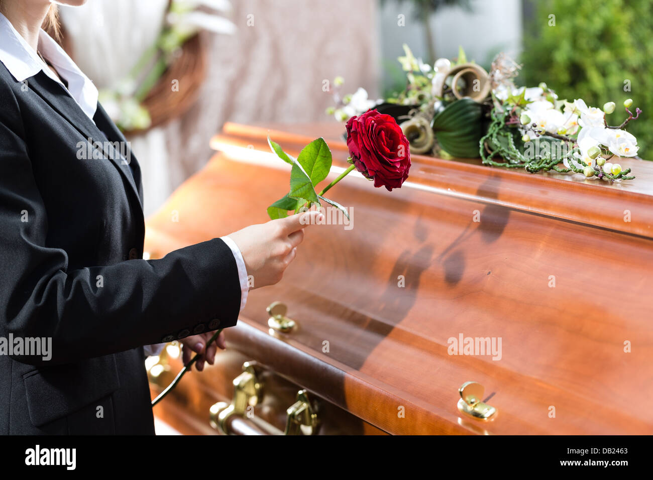 Mourning woman on funeral with red rose standing at casket or coffin ...