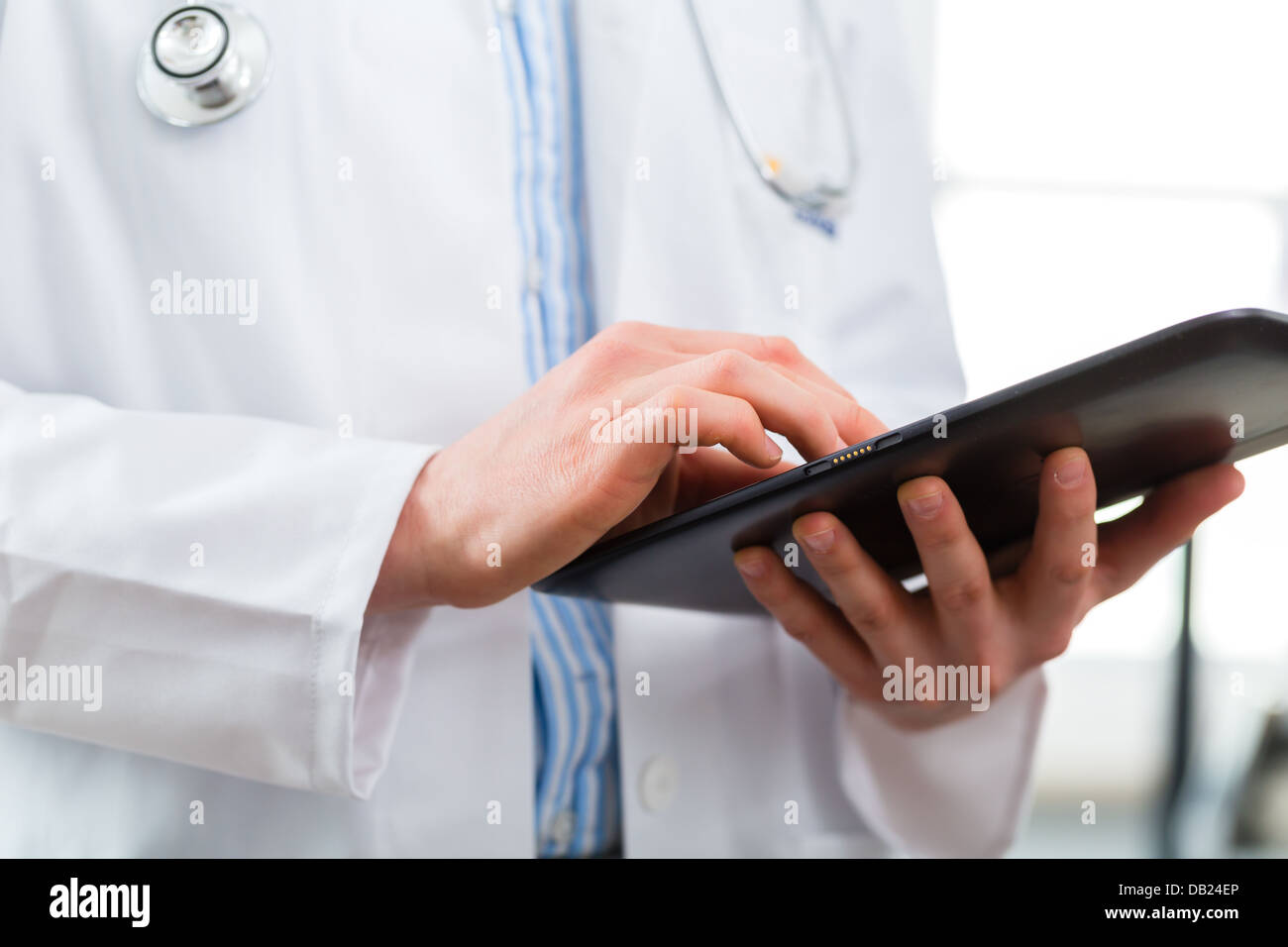 Young doctor standing in clinic reading a file or dossier on the tablet ...