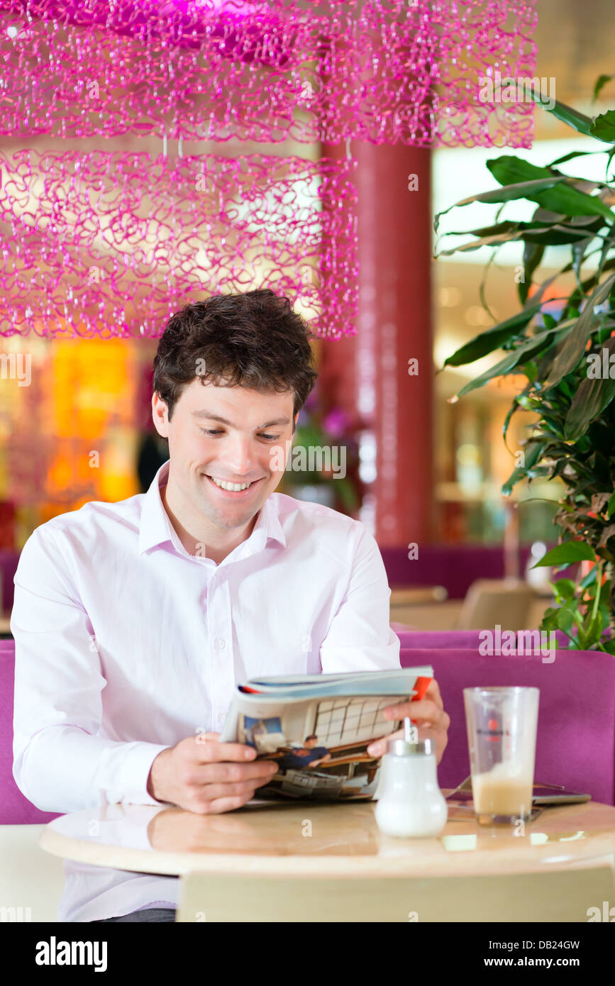 Young man in a cafe or ice cream parlor reading a magazine, maybe he is ...
