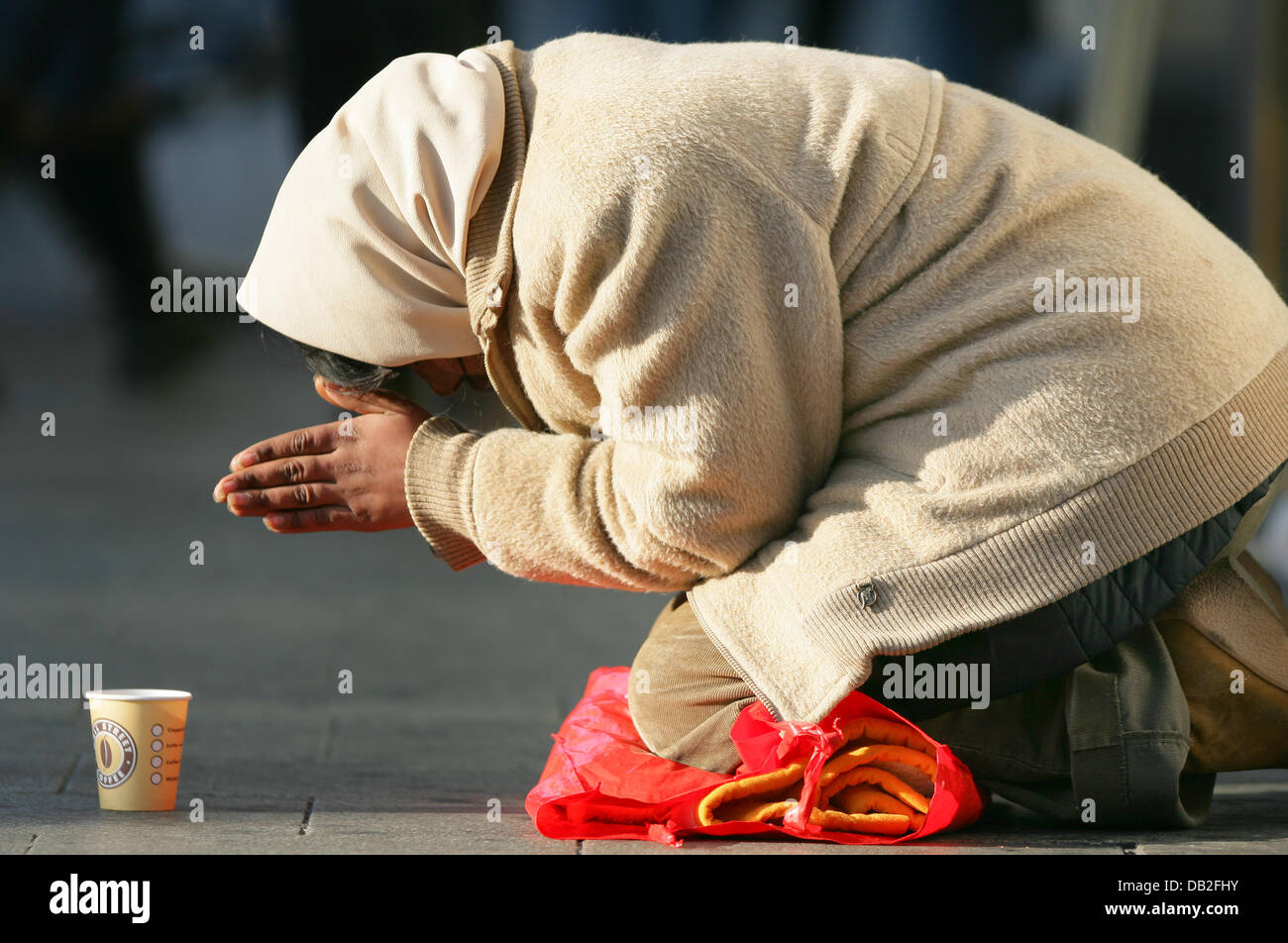 A woman kneels and begs for some money in a shopping street in ...