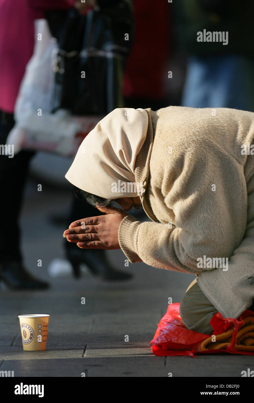 A woman kneels and begs for some money in a shopping street in ...