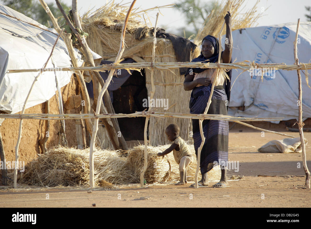 A refugee woman from Chad stands with her child in front of a hut in a ...