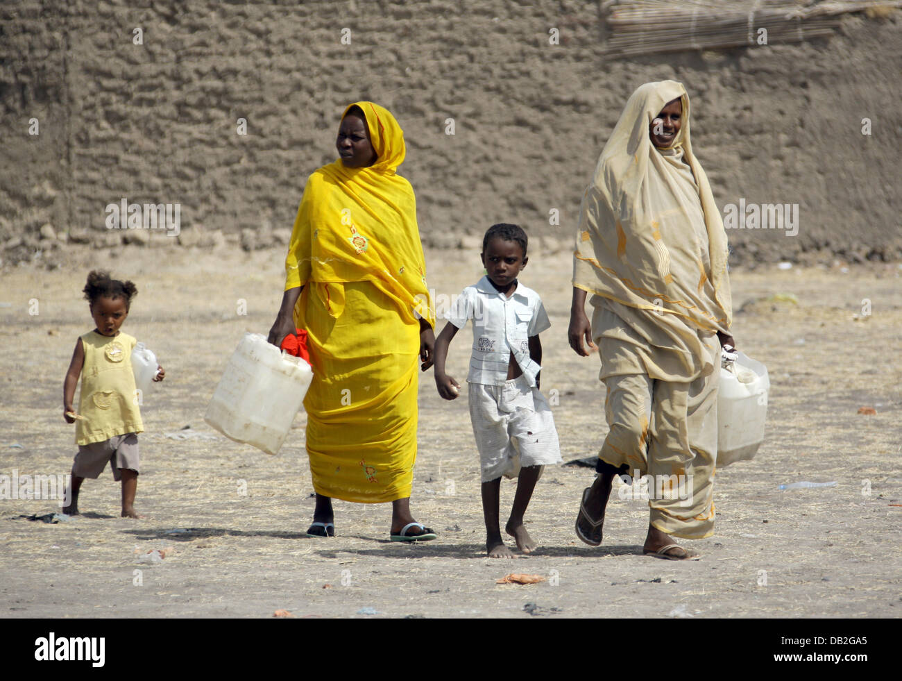 Sudanese women carry water canisters as they walk past ruins and ...