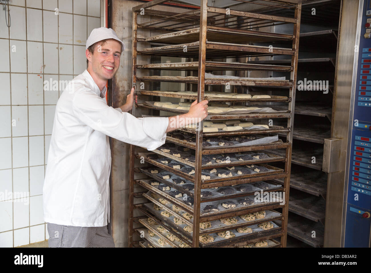 Baker in bakery or bakehouse putting rack with bread, baguettes and ...