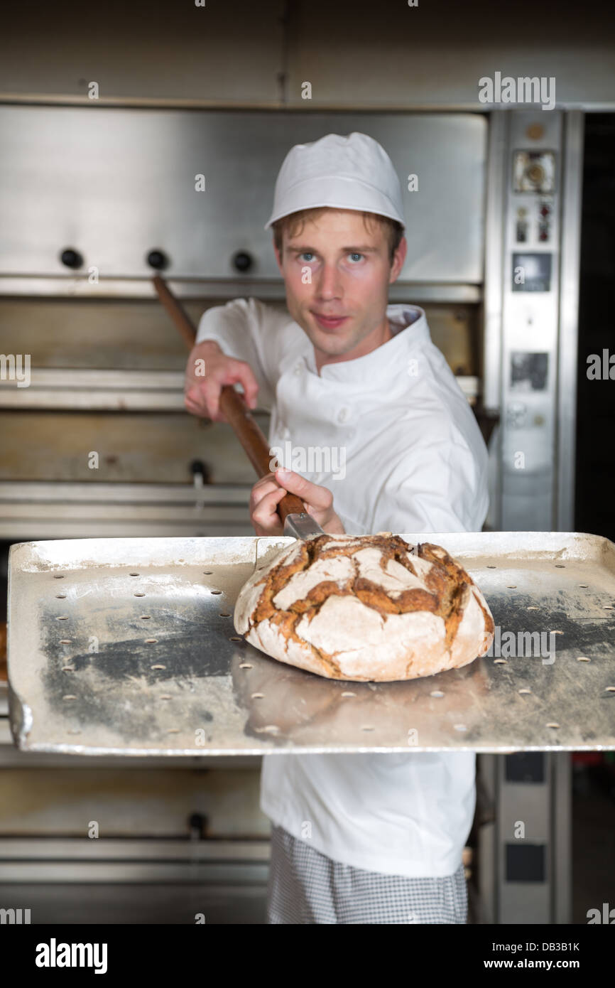 Baker presenting loaf of bread on a peel inside bakery at the oven ...